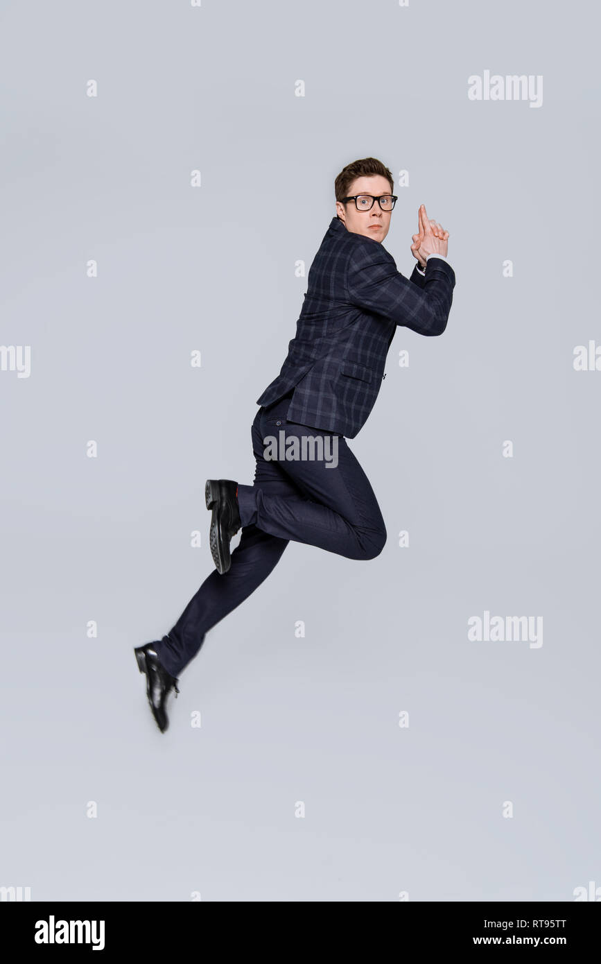 stylish businessman jumping with hand gun gesture isolated on grey ...