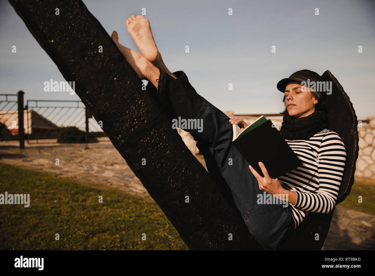 Side view of elegant lady in cap reading volume and sitting on abstract ...