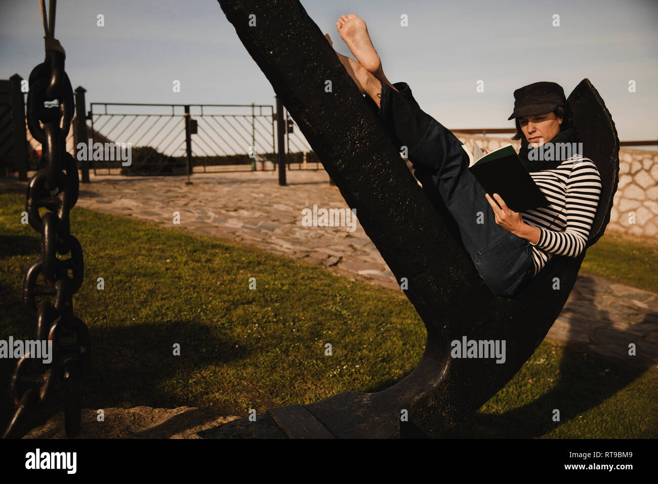 Side view of elegant lady in cap reading volume and sitting on abstract ...