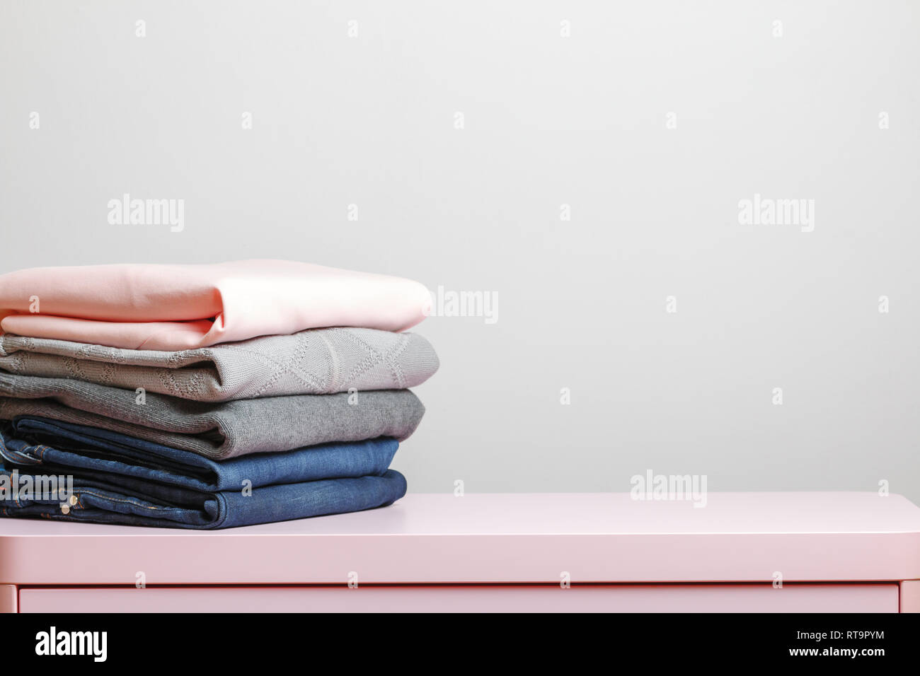 On a pink table is a stack of folded clothes. Gray background. Close-up ...