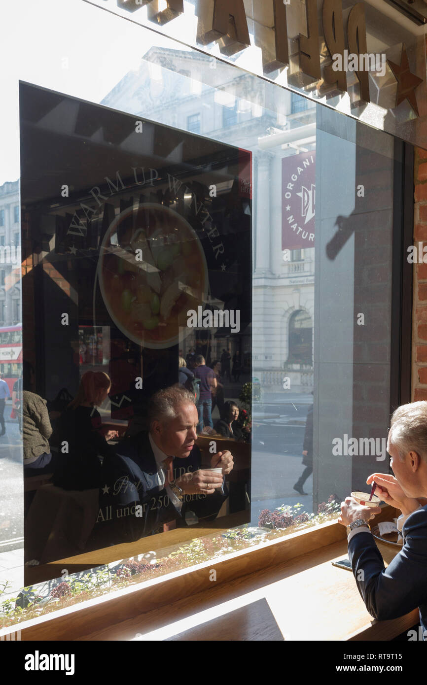 A man eats his lunch in the sunlit window of a Pret a Manger, on 25th ...