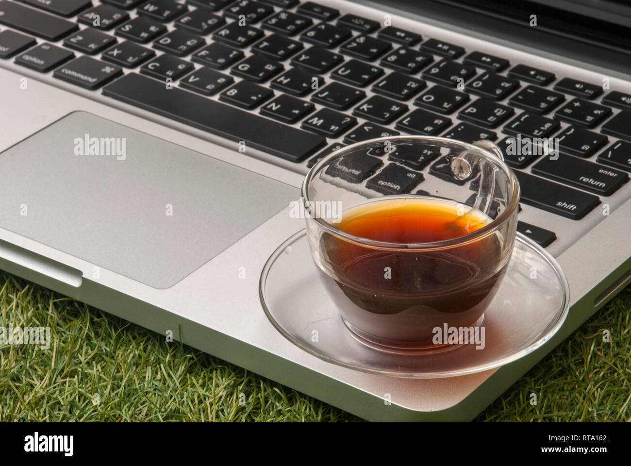 One cup of tea is placed on a laptop in a relaxed lawn area Stock Photo ...