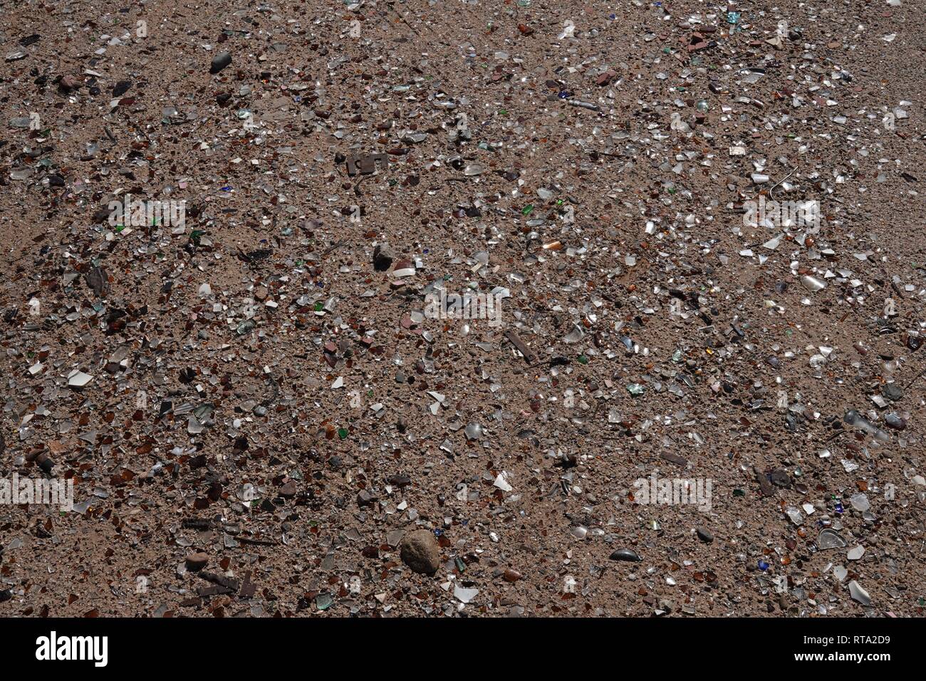 A bunch of broken glass from multiple bottles on the desert sand in the ...
