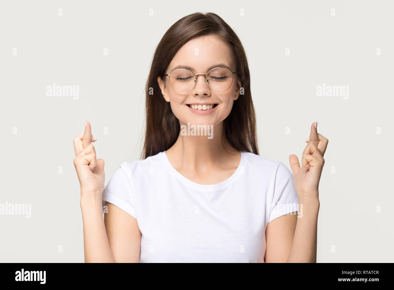 Happy hopeful girl making wish crossing fingers isolated on background ...