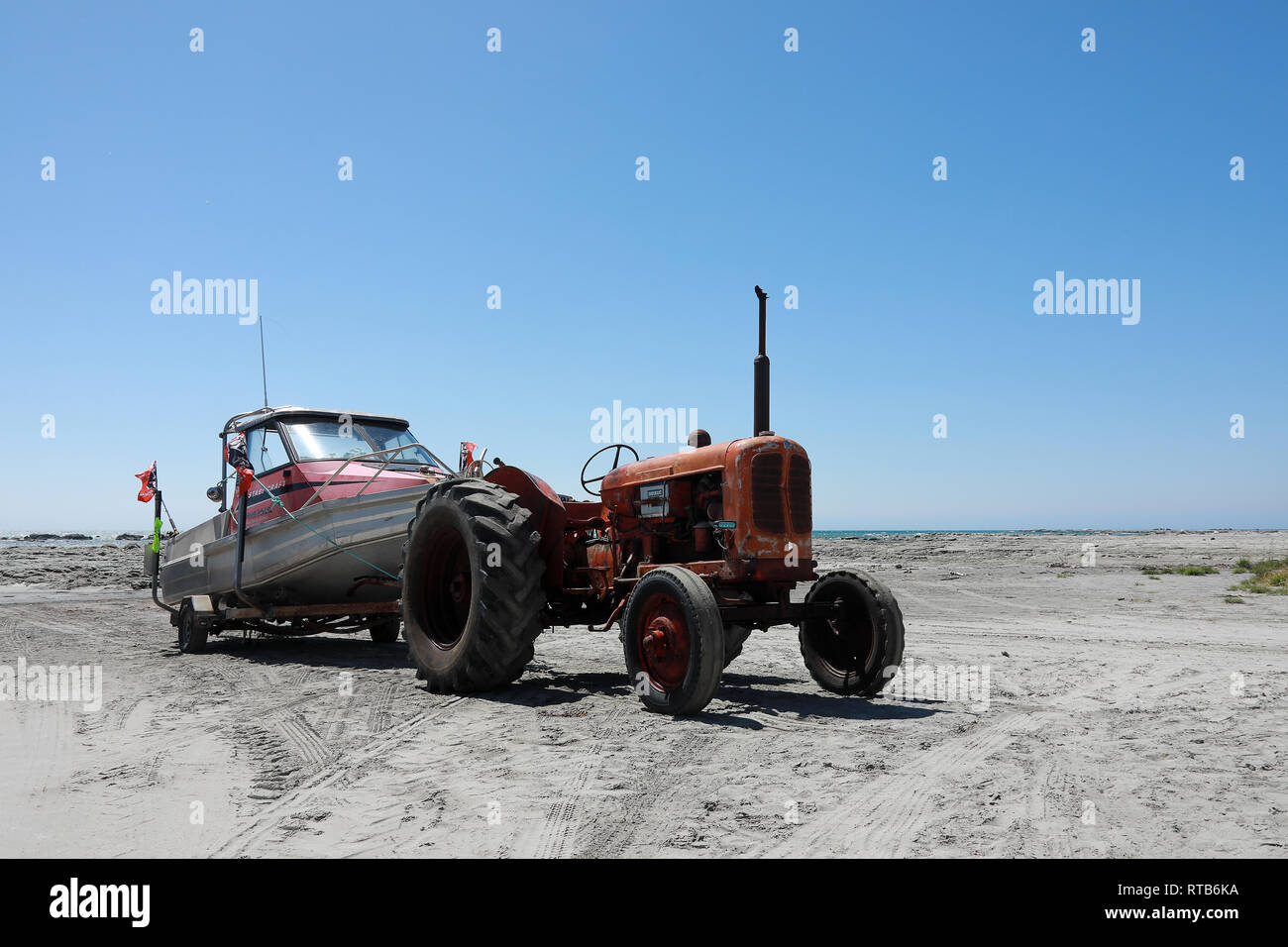 Small lobster fishing boat on a trailer on a beach with towing tractor ...