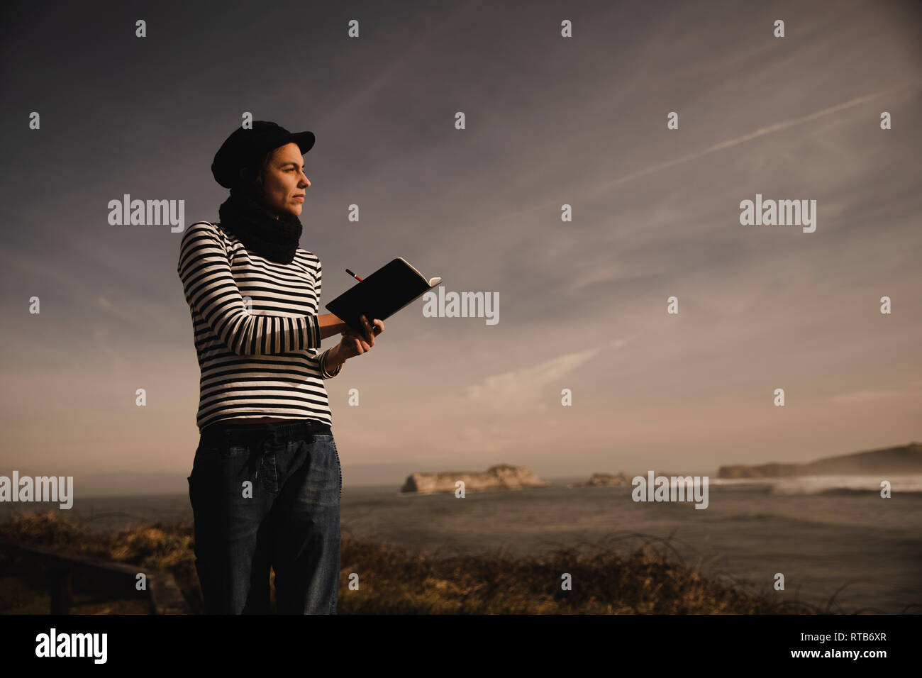 Elegant lady in cap taking notes in notepad on seat on coast near ...