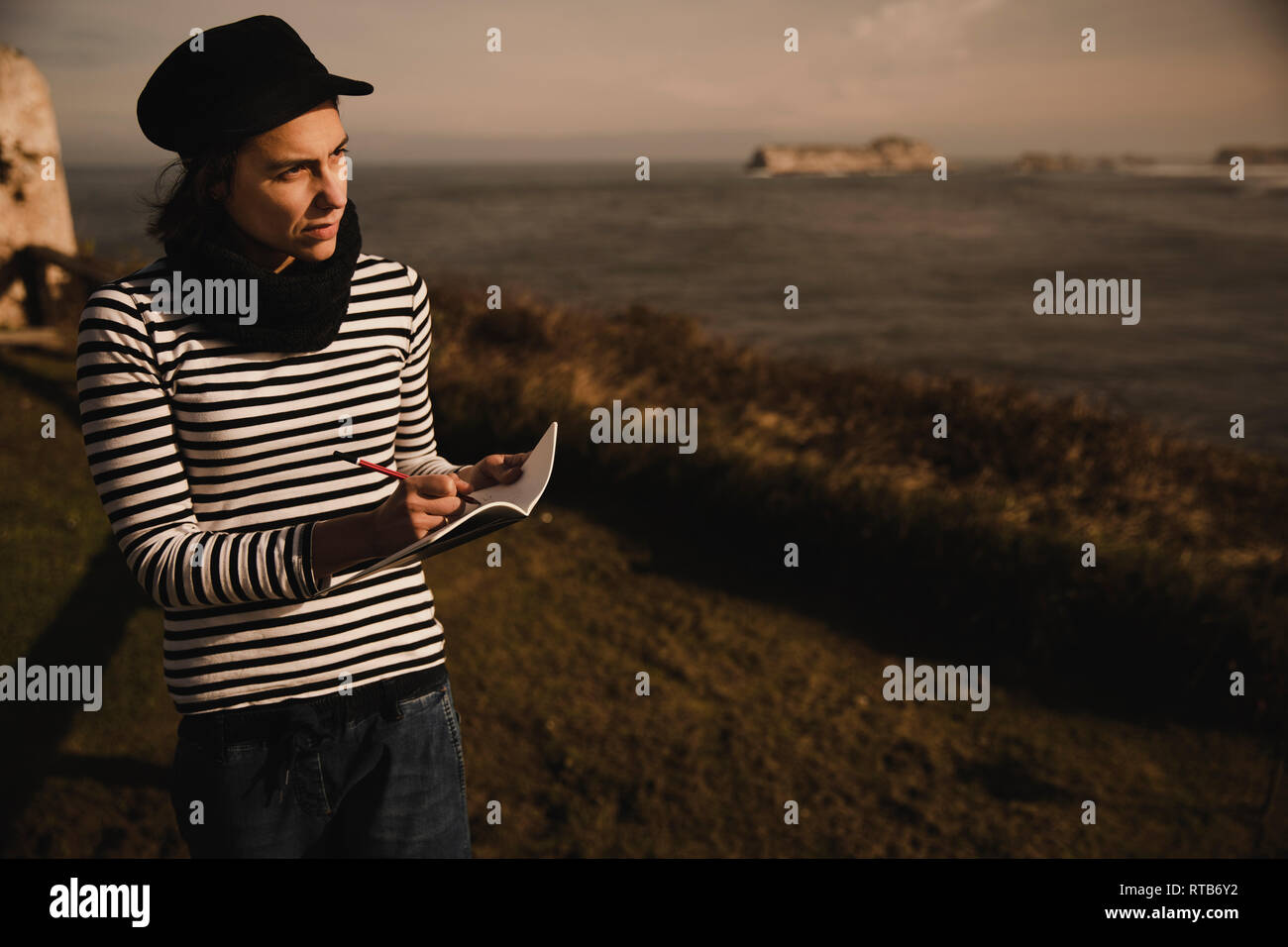 Elegant lady in cap taking notes in notepad on seat on coast near ...