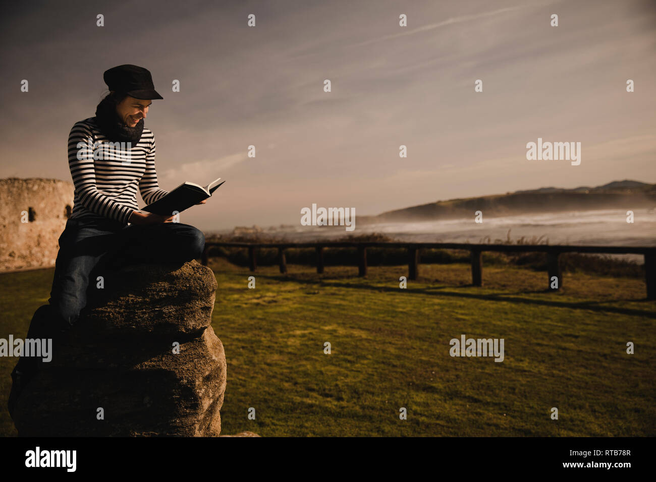 Elegant lady in cap sitting on seat on coast near waving sea Stock ...