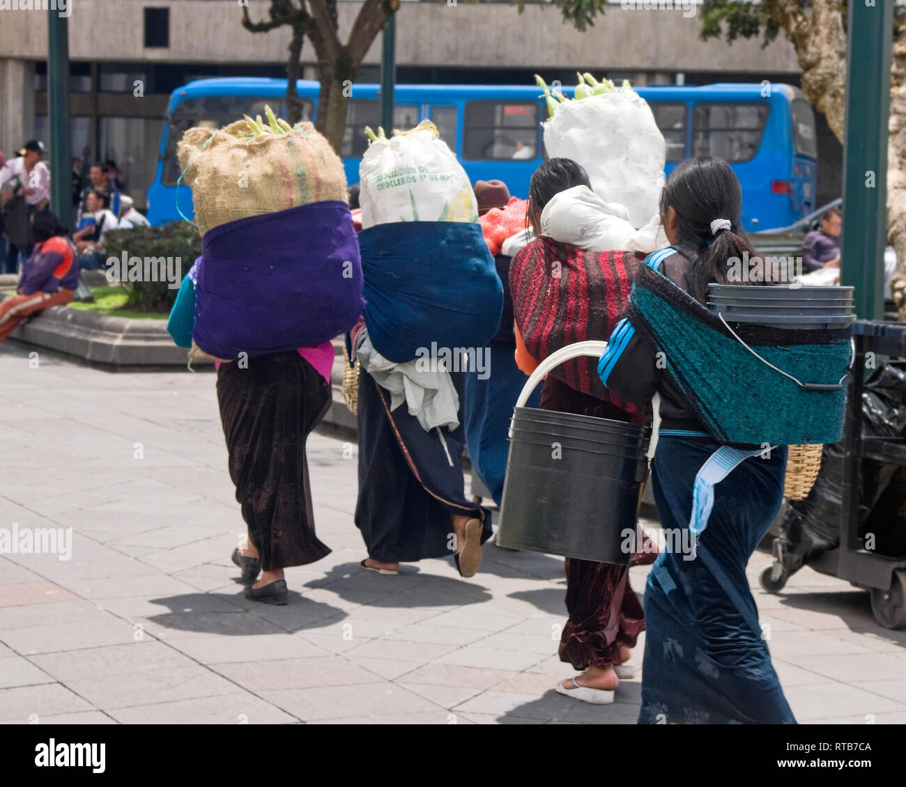 Indigenous women walking, carrying large sacks on backs; heavy load ...