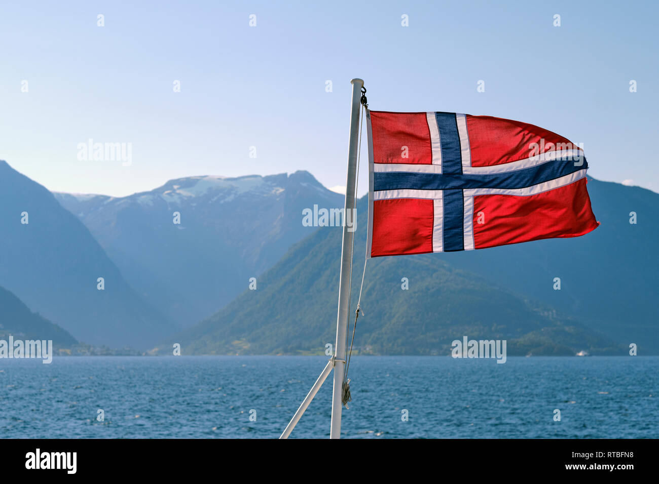 A Norwegian flag flying in the sun and blue sky fjord and mountain ...