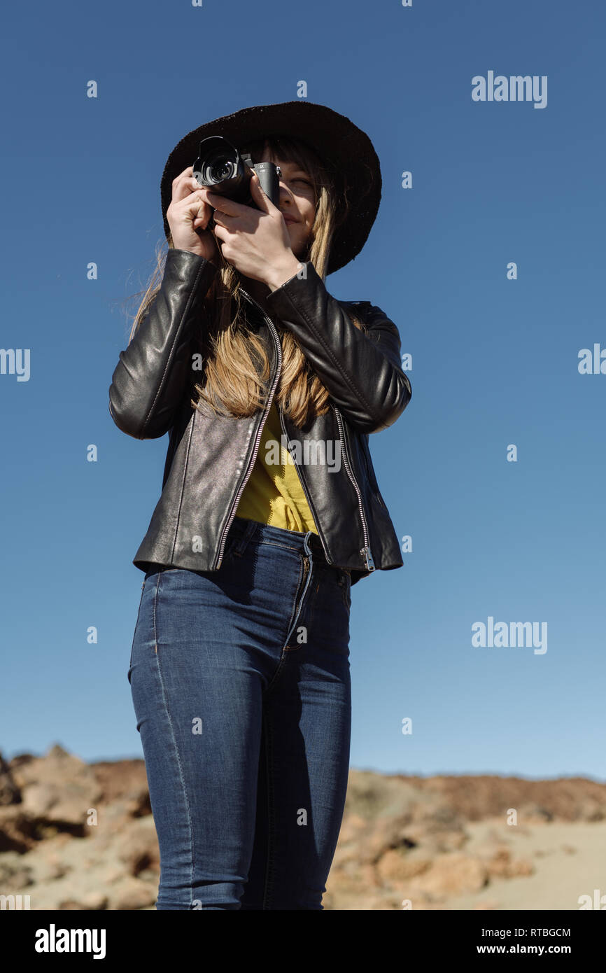 Female photographer standing with camera and looking at hills in desert ...