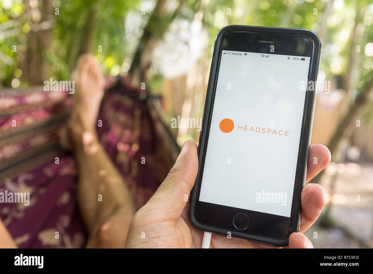 A man lying in a hammock using an iPhone showing the app Headspace ...