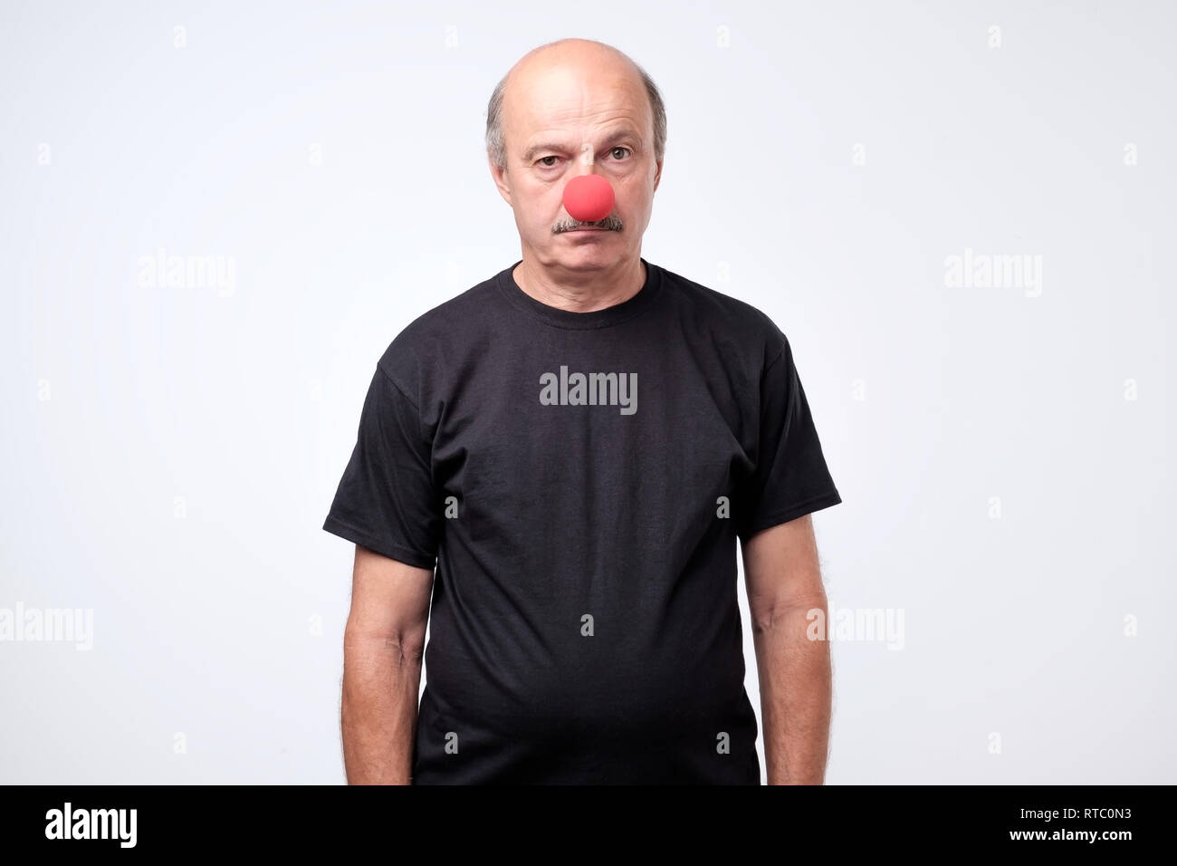 Mature man wearing clown nose isolated on white background. He is sad ...