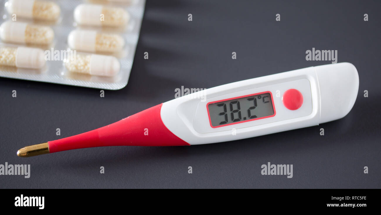 Red fever thermometer with digital display and pills lying on the desk ...