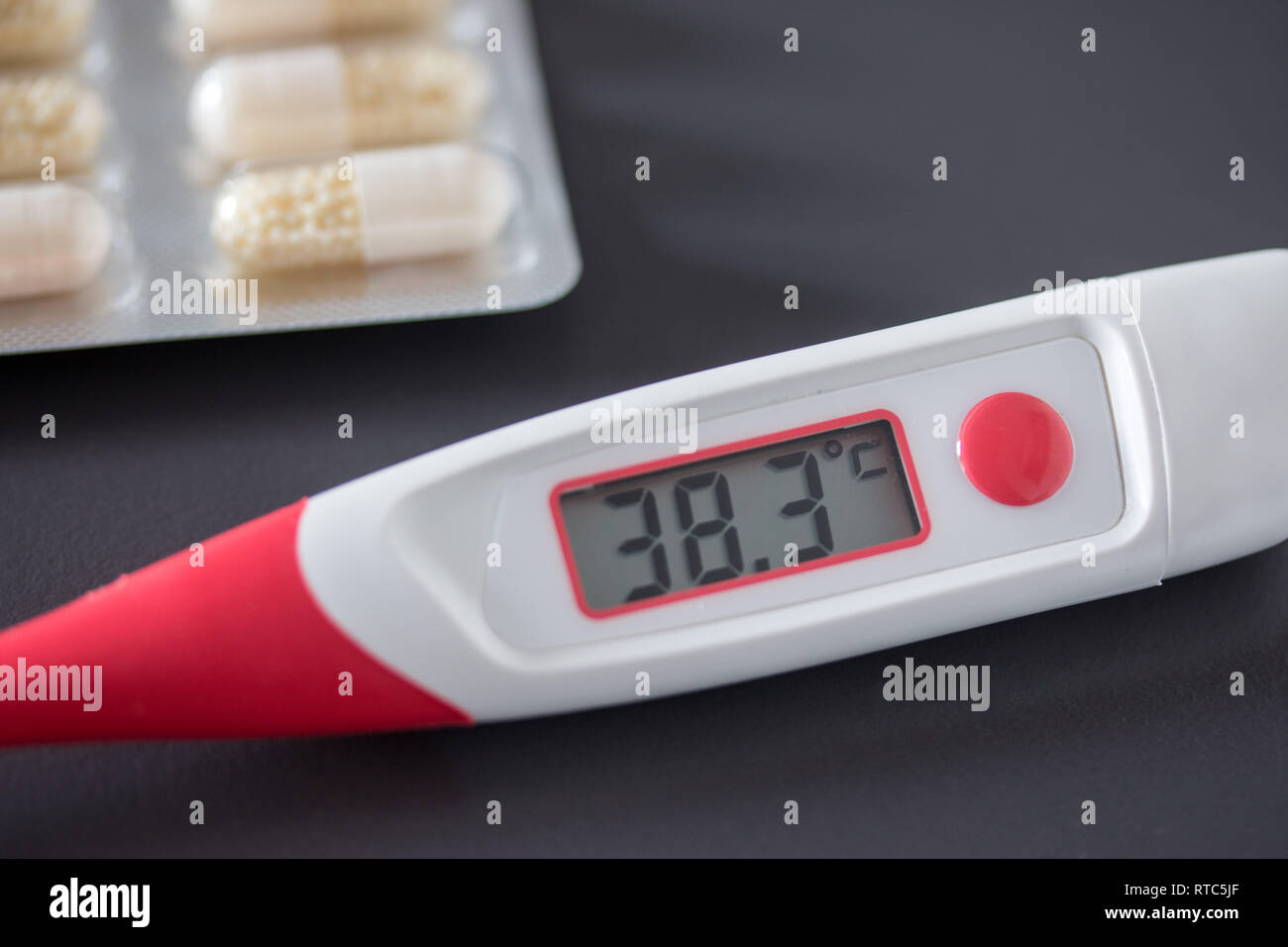 Red fever thermometer with digital display and pills lying on the desk ...