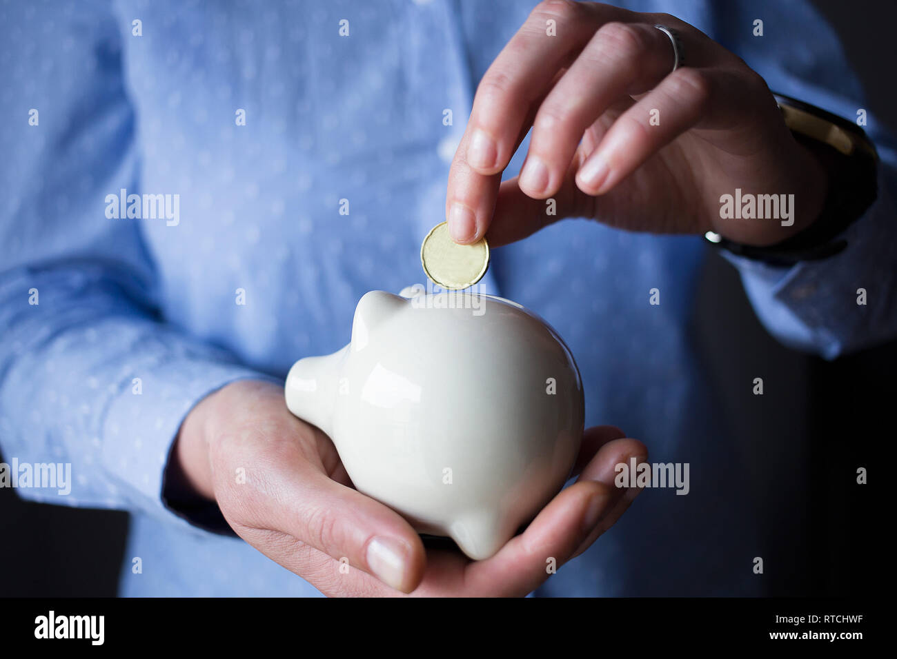 Person is inserting a golden coin into a black ceramic piggy bank Stock ...