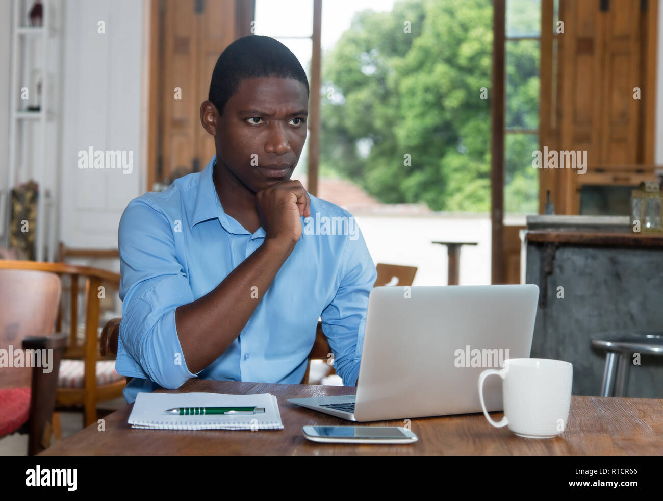 Thinking african american man with laptop at home at desk Stock Photo ...