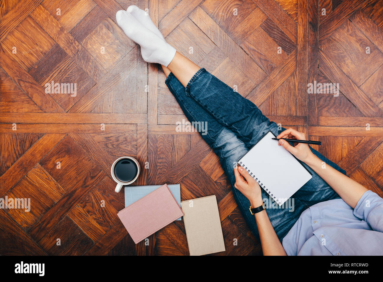 View from above young female sitting on wooden floor writing in notepad ...