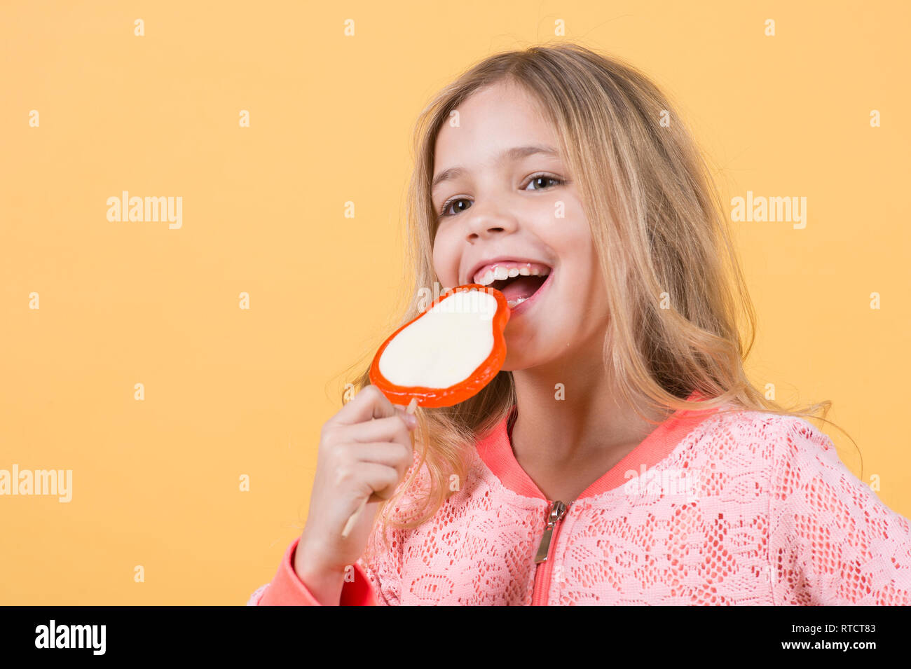 Child eat candy on stick. Girl smile with lollipop on orange background ...