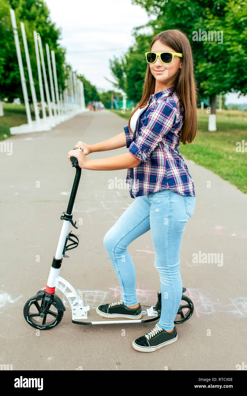 Girl schoolgirl teenager 10-15 years. On a scooter in summer city park ...