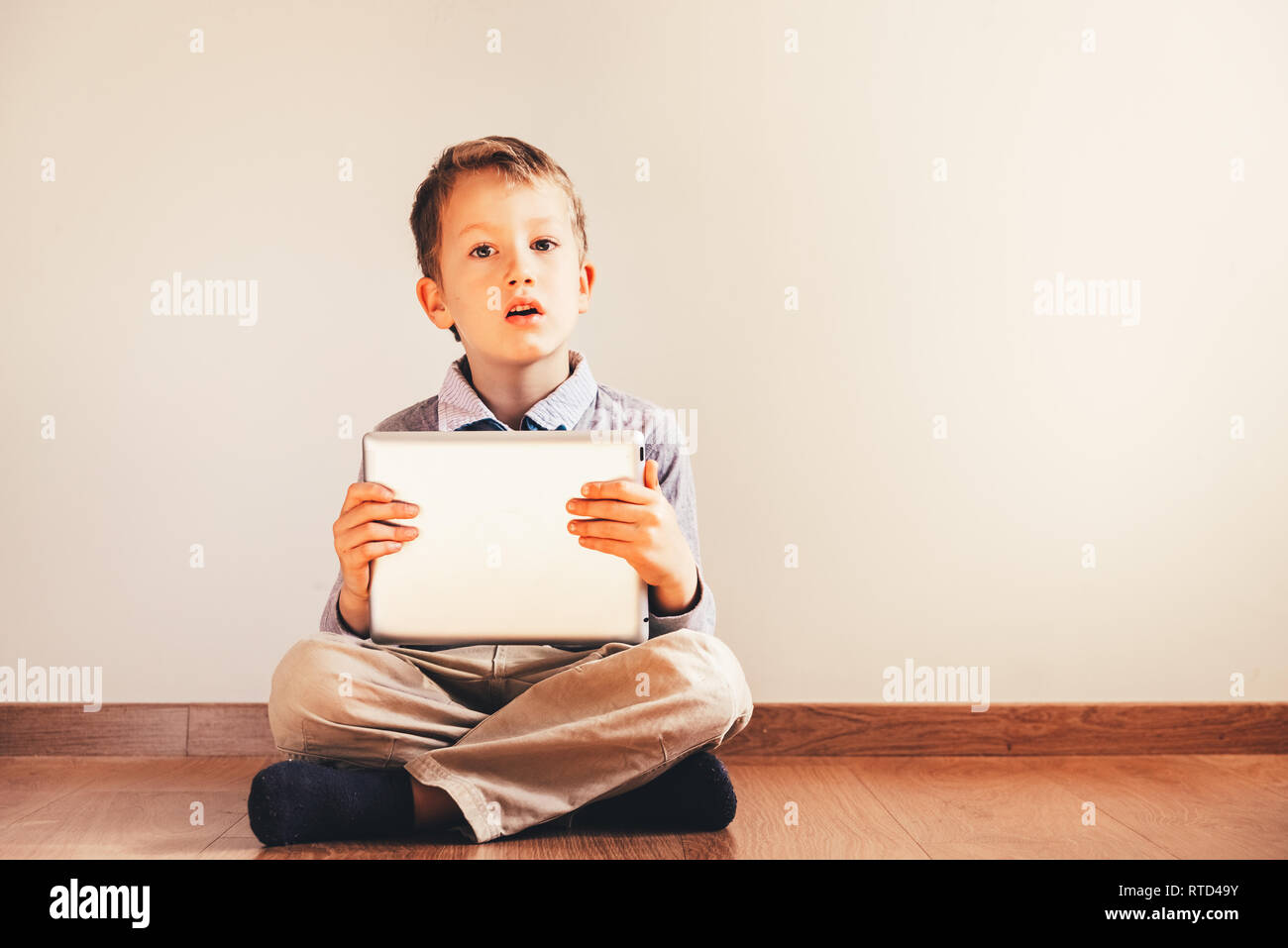 Boy sitting on the floor with a digital tablet in his hands, using it ...