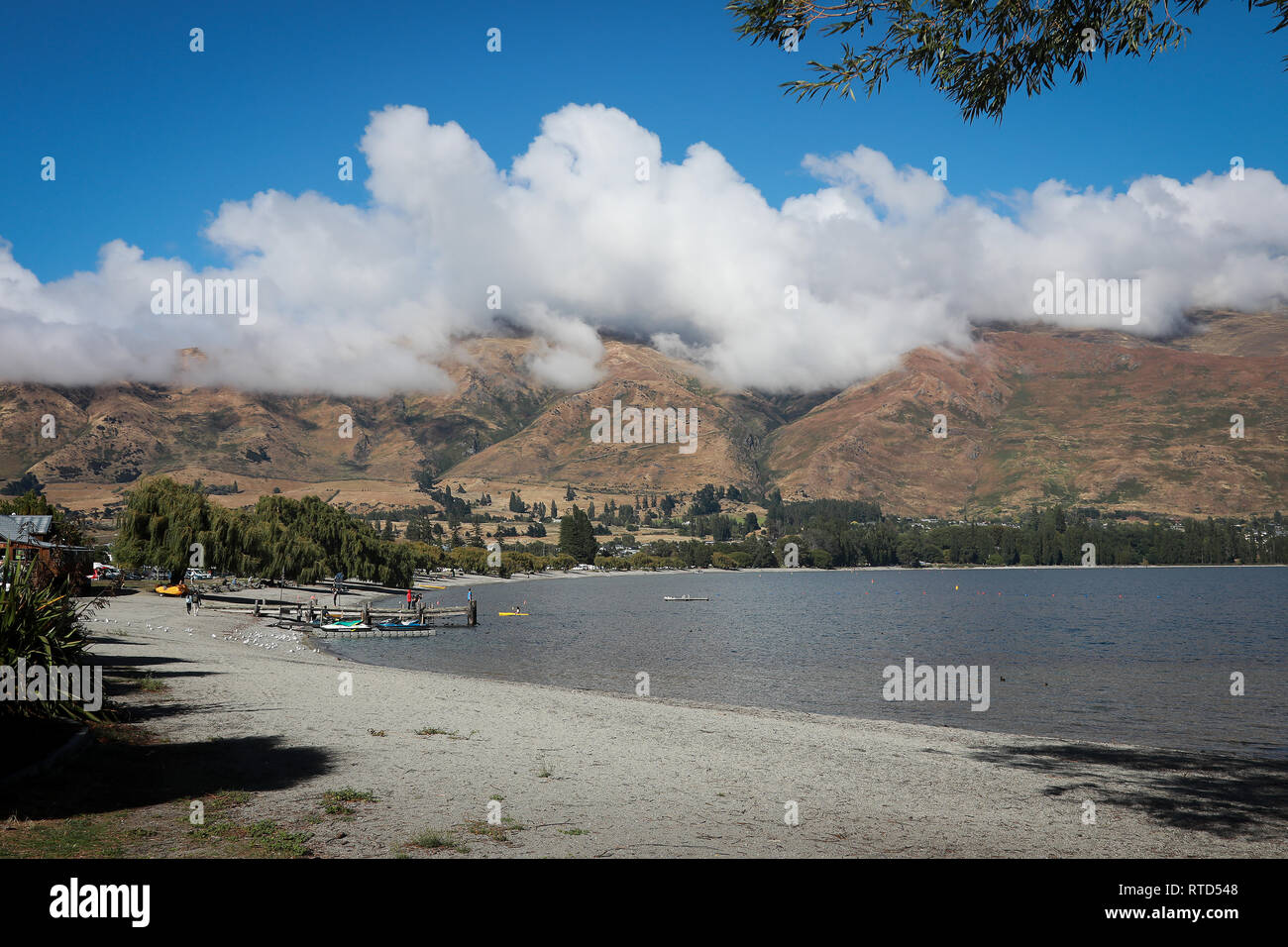 Pebble beach on Lake Wanaka on sunny summers day with clouds over the ...