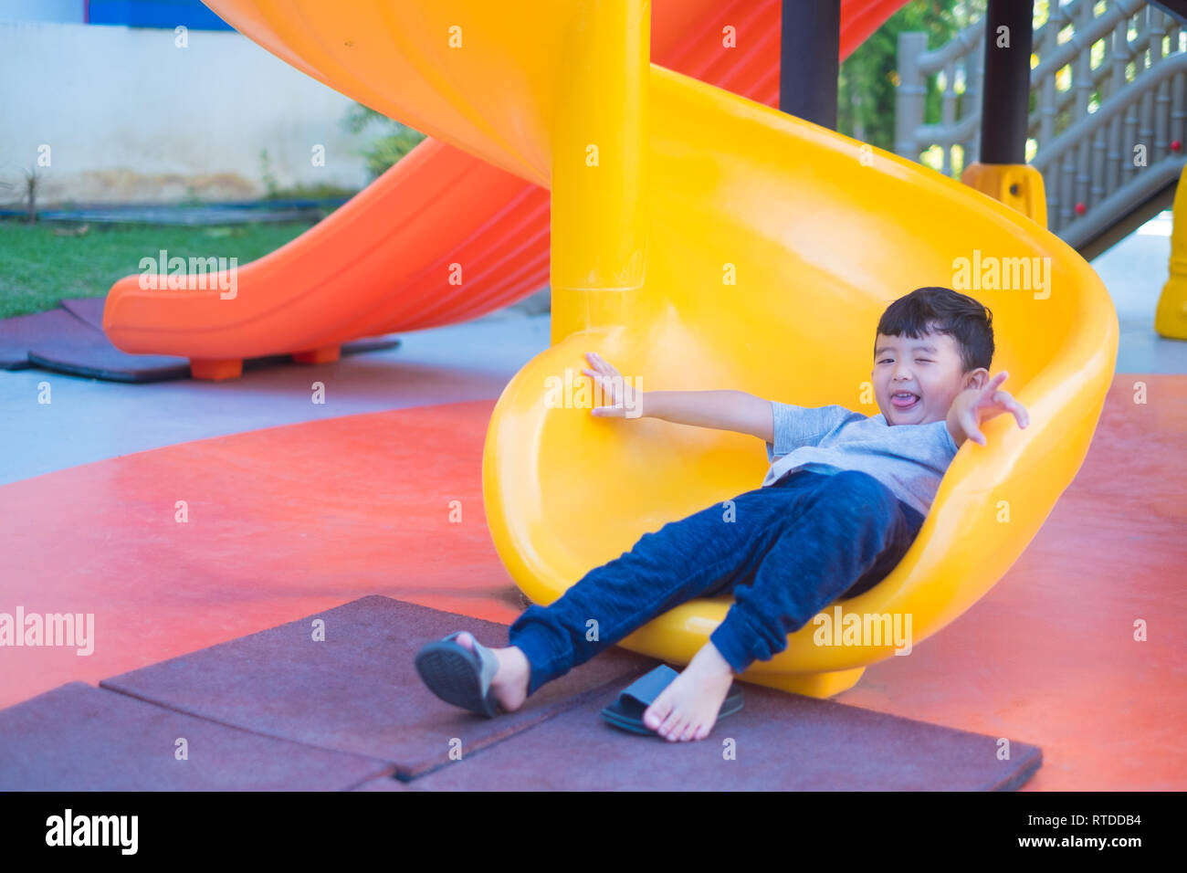 Asian kid playing slide at the playground under the sunlight in summer ...