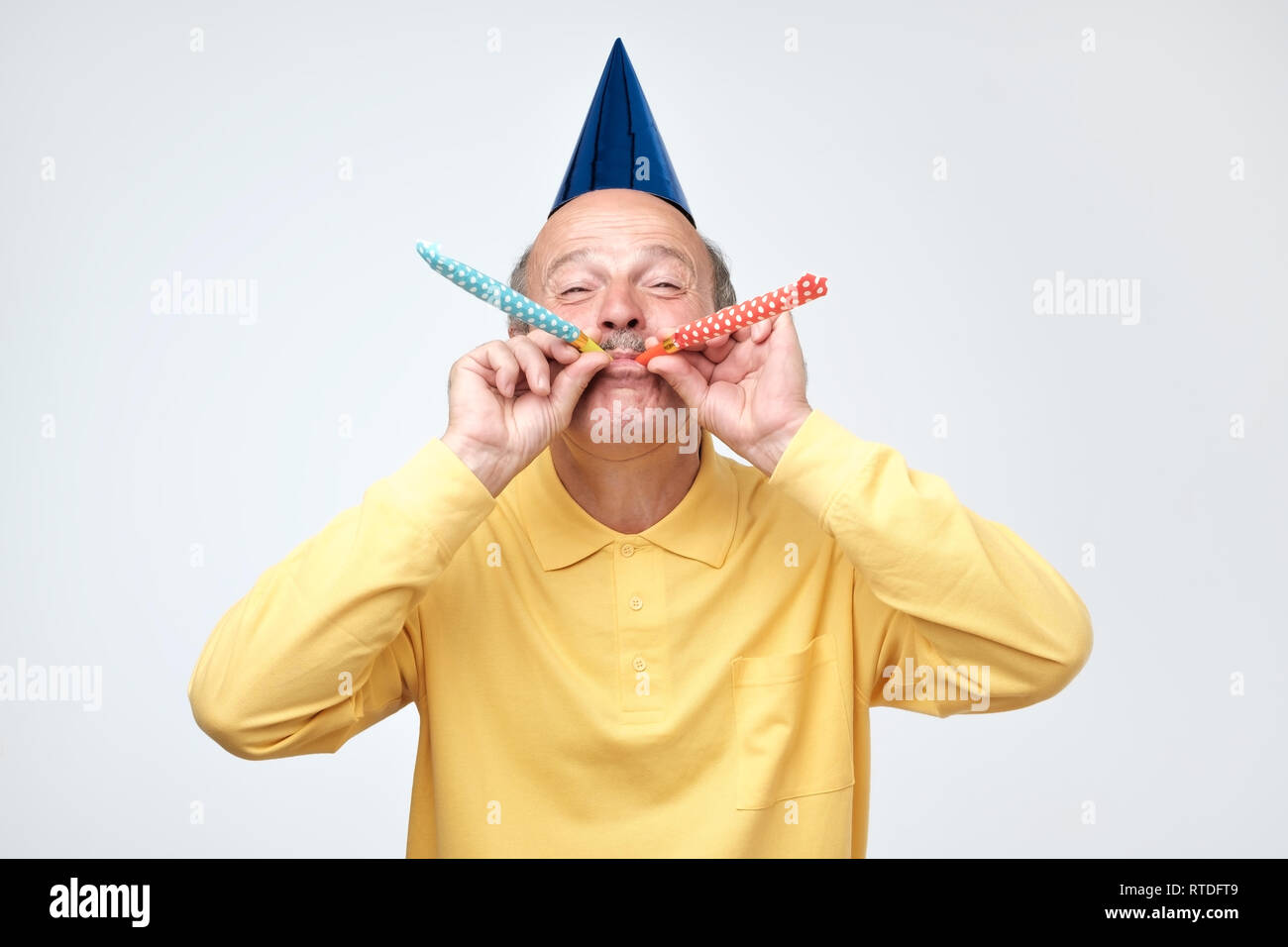 Senior european man blowing party horn and staring at camera having ...