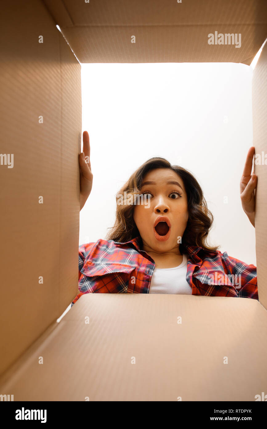 Smiling young woman opening a carton box, relocation and unpacking ...