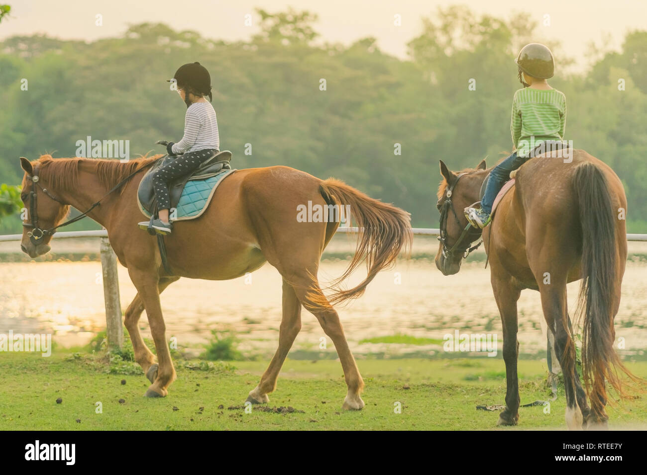 Kids learn to ride a horse near the river before sunset Stock Photo - Alamy