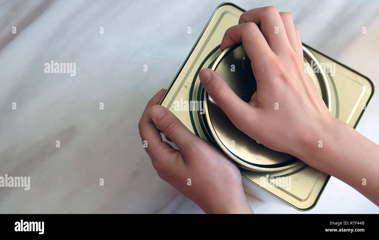 Hands holding to a square tin can and prying open the lid, from the ...