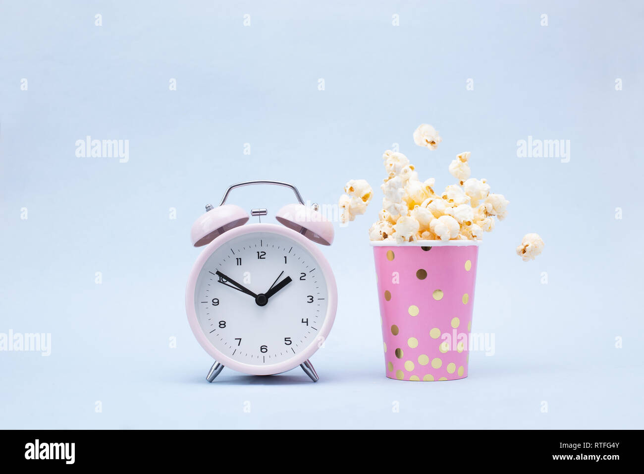 Flying Popcorn in a bright glass and a ringing alarm clock on a blue ...
