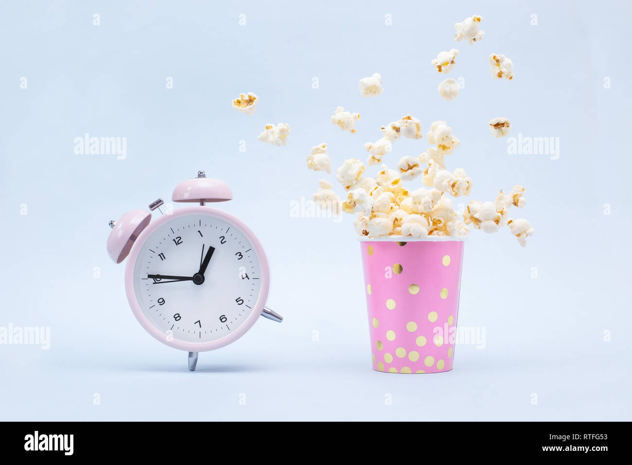 Flying Popcorn in a bright glass and a ringing alarm clock on a blue ...