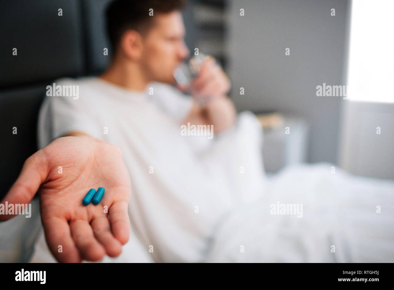 Young man in bed early morning. He hold two capsules on palm. Drink ...