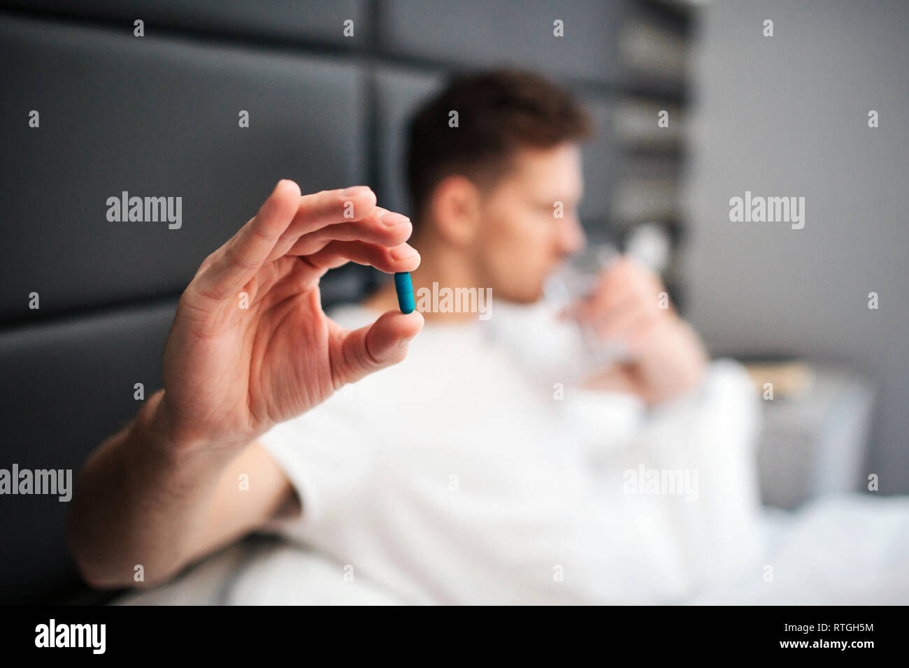 Young man in bed early morning. He hold blue capsule between tow ...
