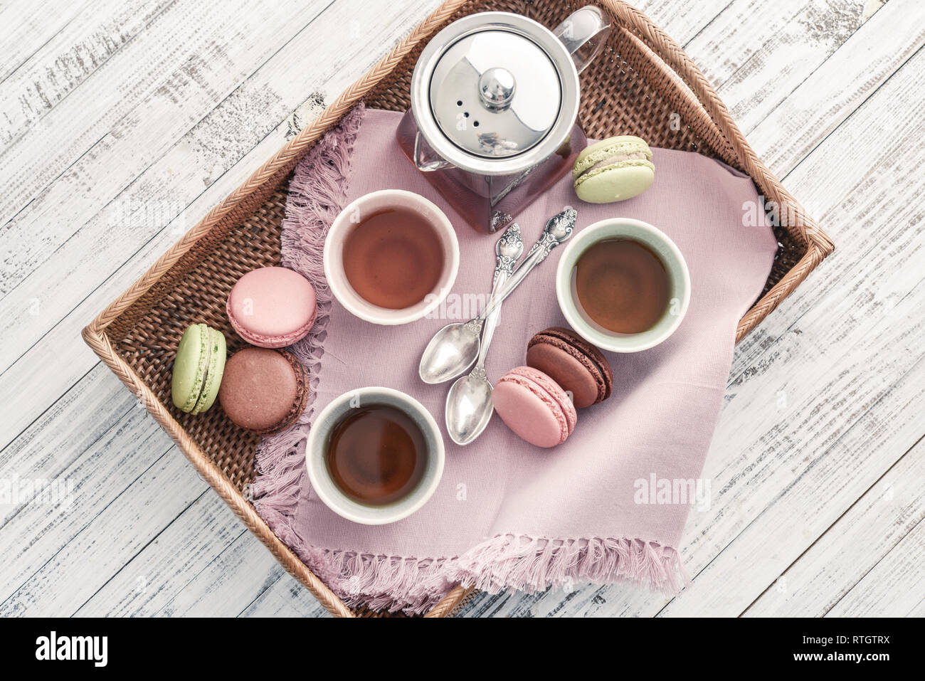 Different kinds of macaroons with glass teapot and cups on rattan tray ...