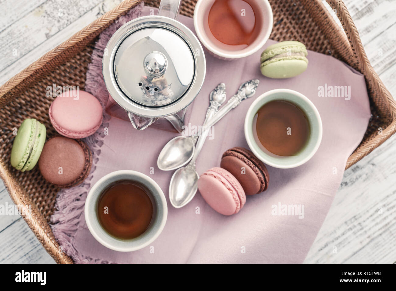 Different kinds of macaroons with glass teapot and cups on rattan tray ...