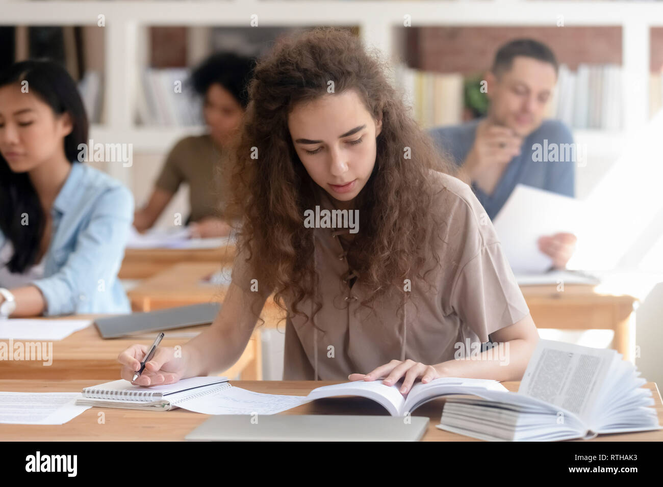 Teen girl studying with textbook writing essay learning in classroom ...
