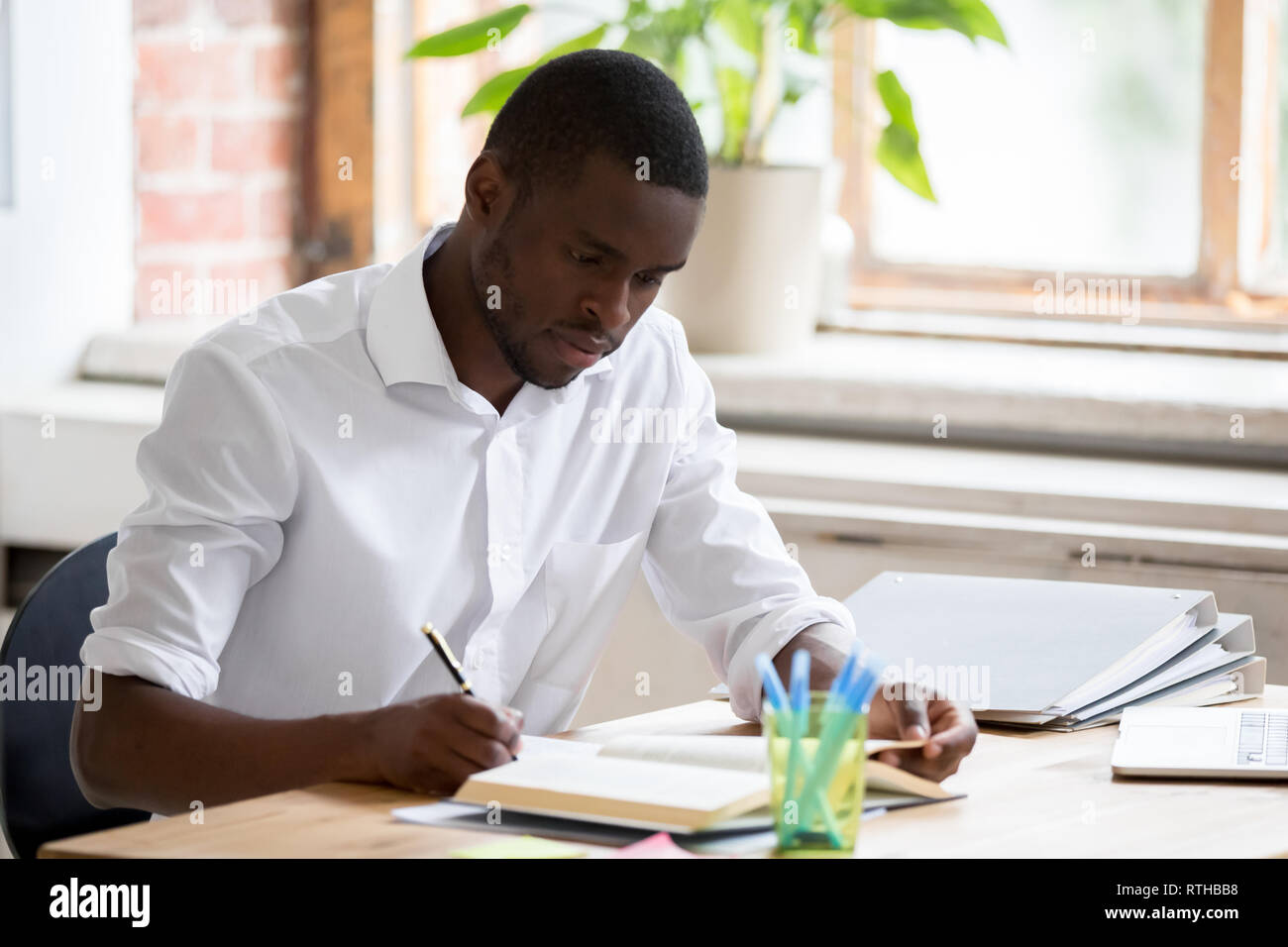 Serious african man university student studying reading textbook making ...