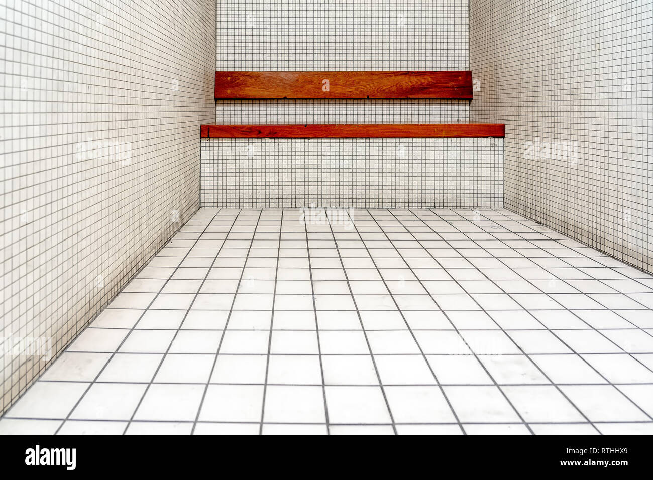 The very sober interior of a prison cell: bare tiled walls and a wooden ...