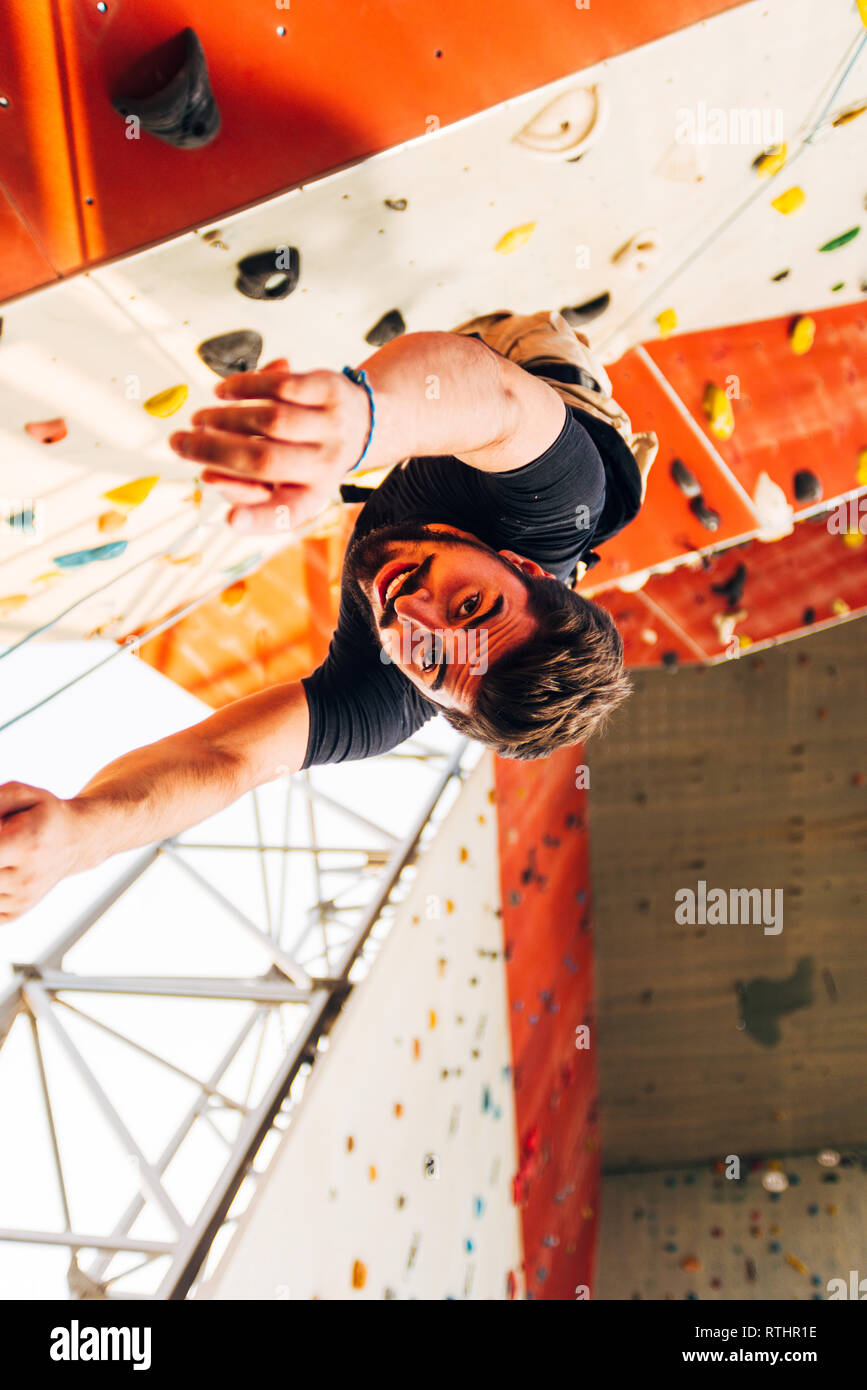 Young climber guy descending on practical rock in climbing center ...