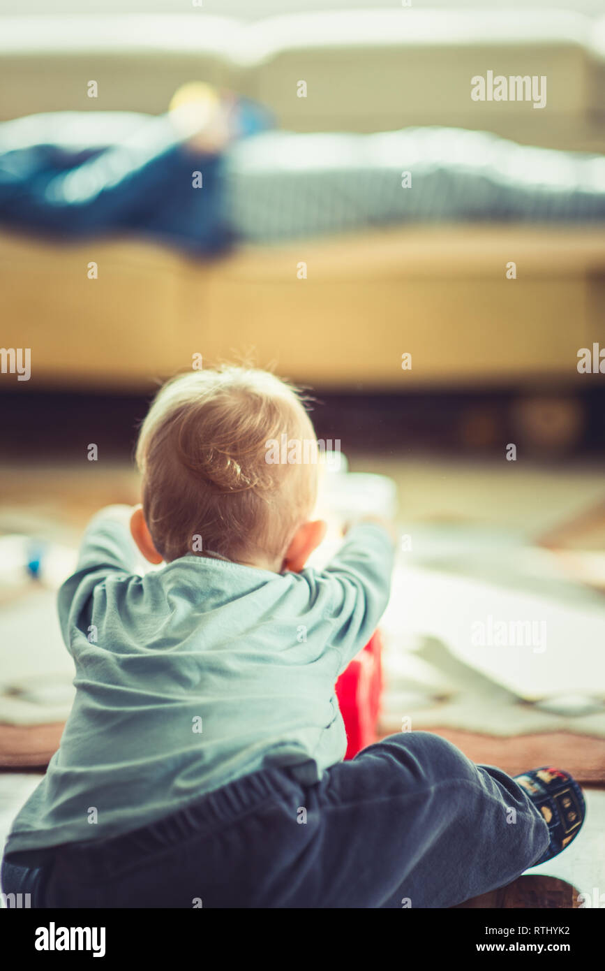A little kid is playing alone in his room while sitting on the ground ...