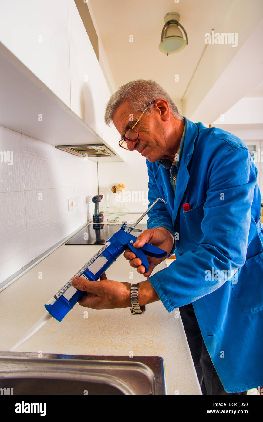Mature handyman is holding caulking gun and working on the basin in the ...
