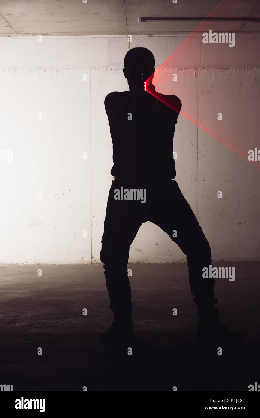 silhouette of an armed man holding his gun and pointing with his laser ...