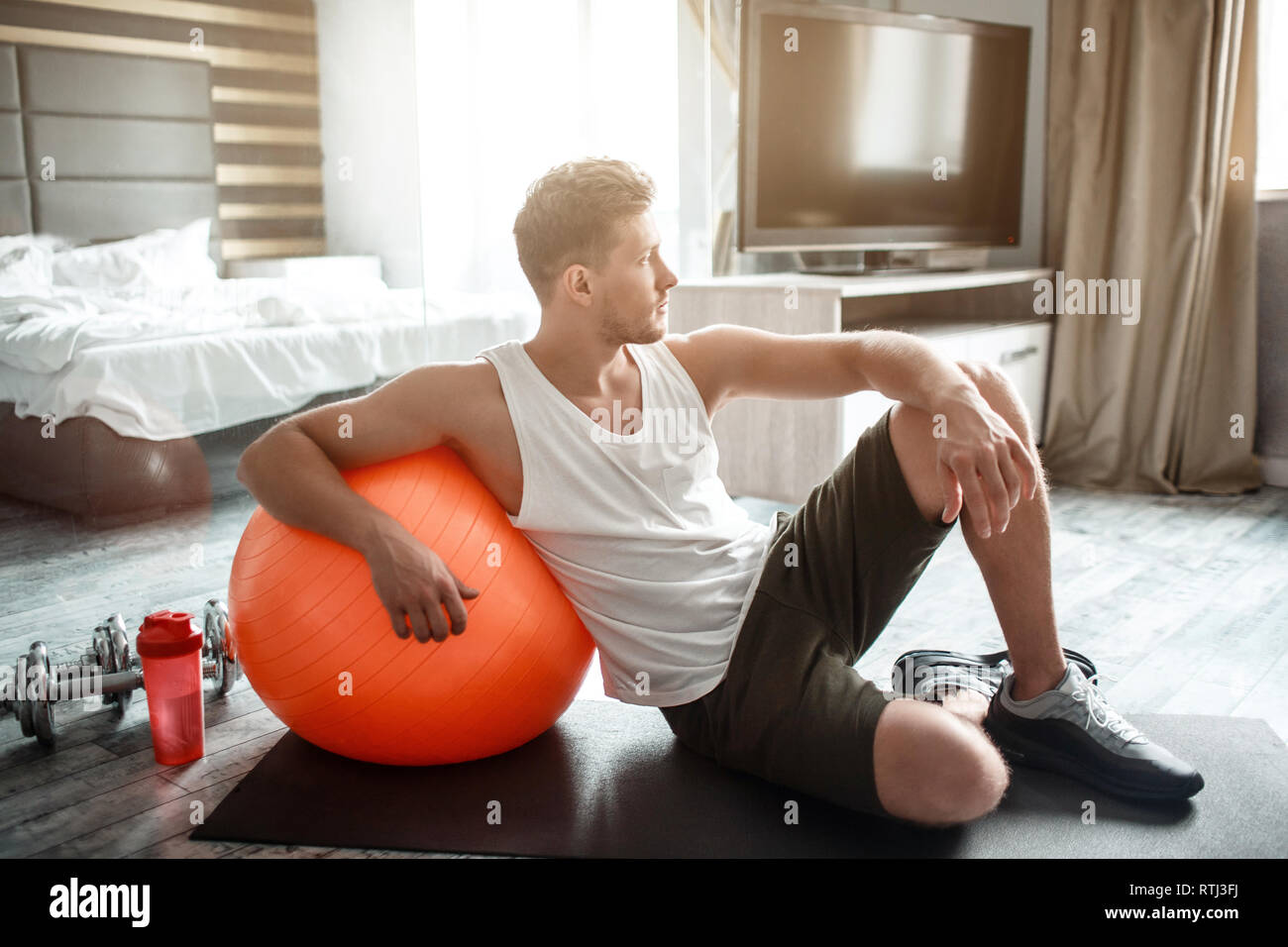 Young well-built man go in for sports in apartment. He lean to big ...