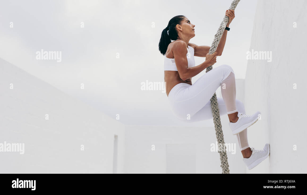 fitness woman doing strength training climbing a wall using a rope ...