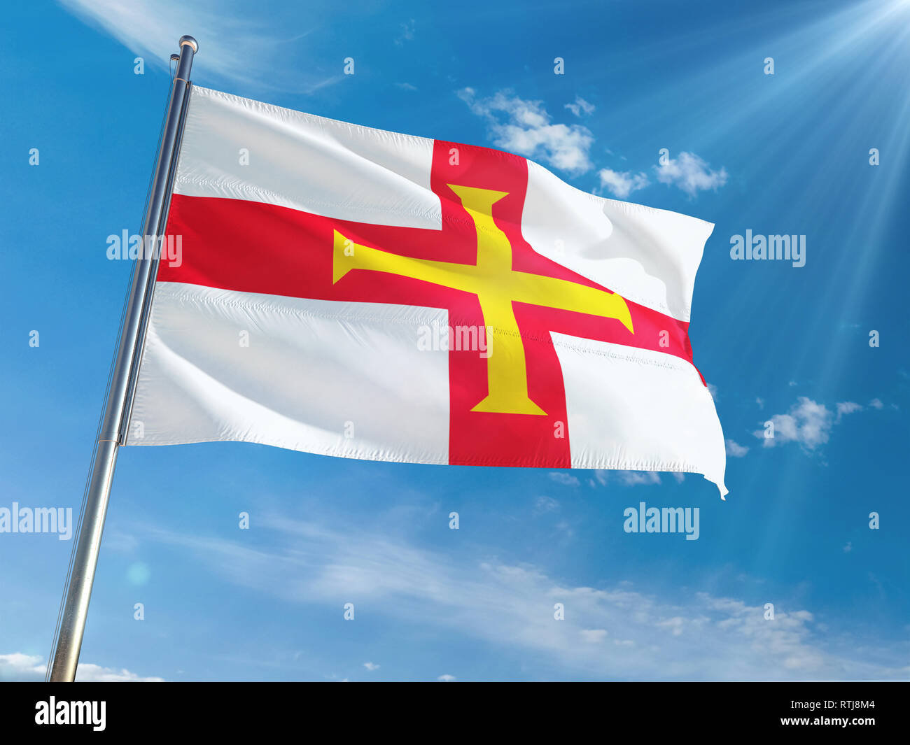 Guernsey National Flag Waving on pole against sunny blue sky background ...
