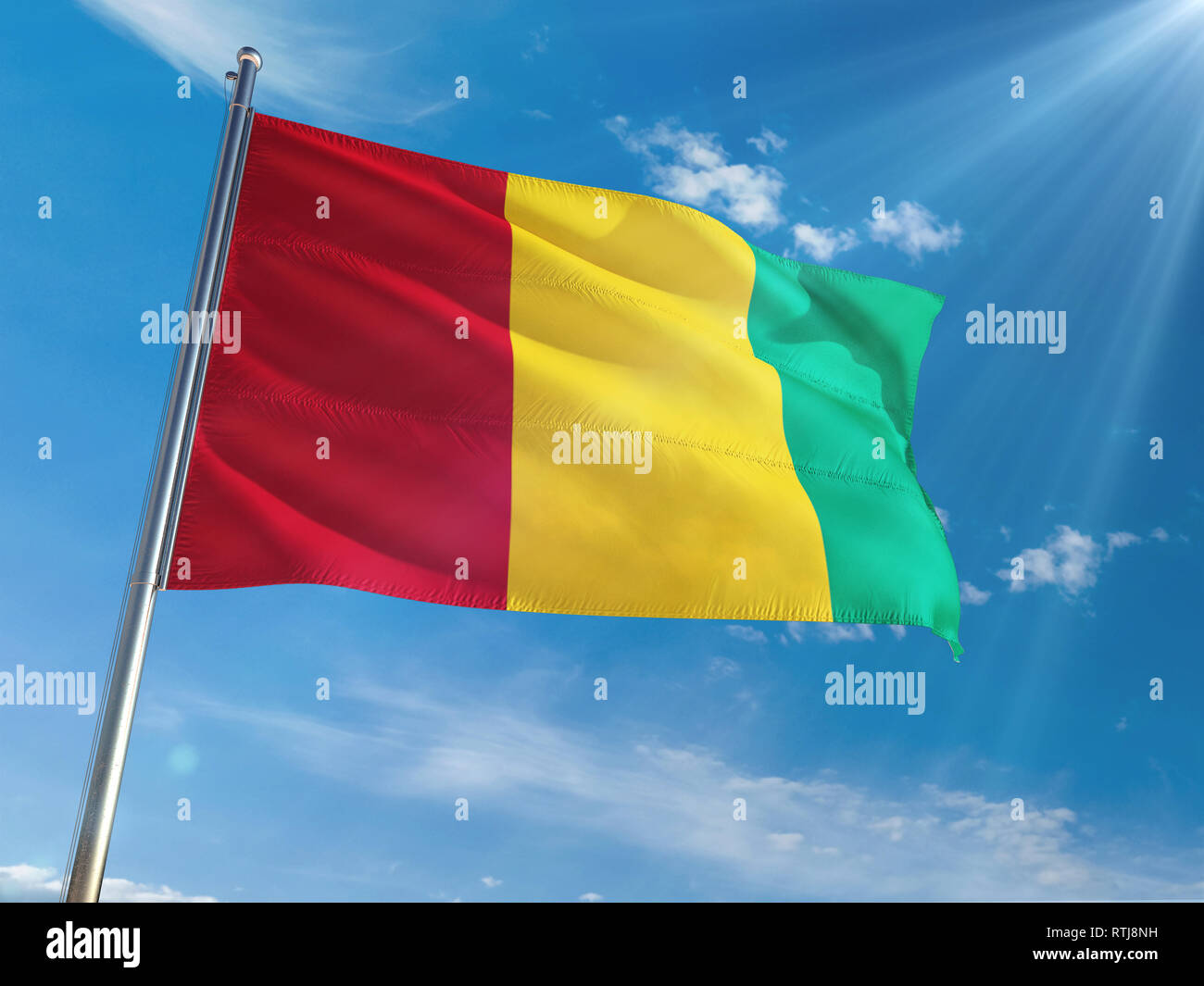 Guinea National Flag Waving on pole against sunny blue sky background ...