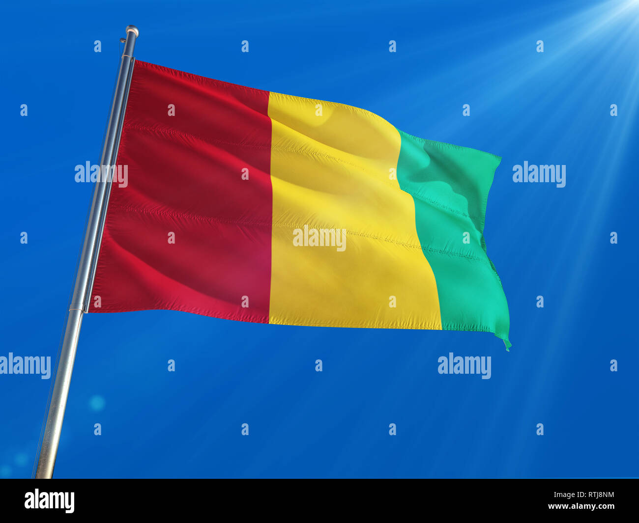 Guinea National Flag Waving on pole against deep blue sky background ...