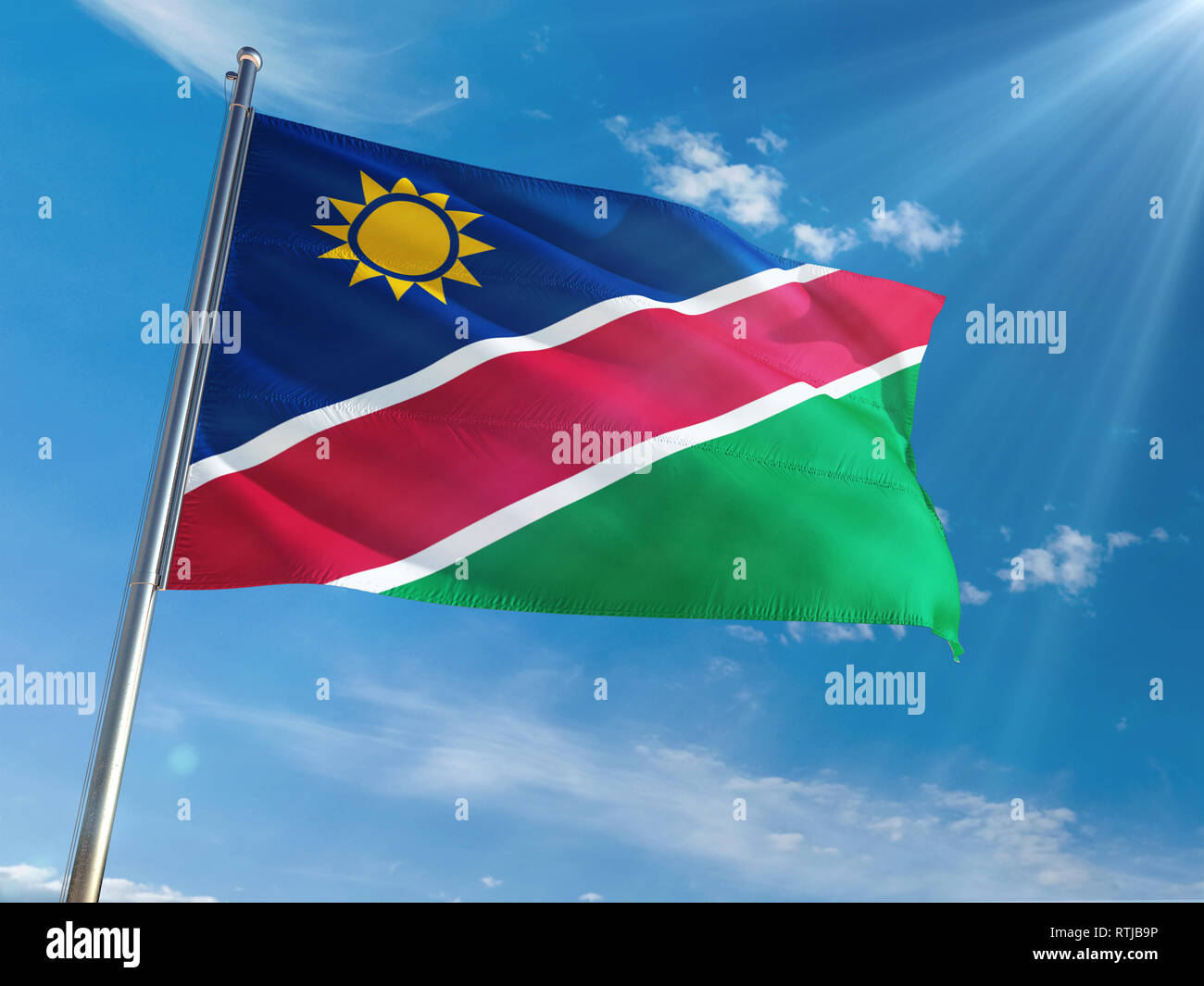 Namibia National Flag Waving on pole against sunny blue sky background ...